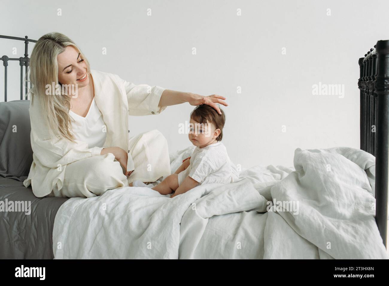Portrait of a little girl sitting next to her mother on the bed in the ...