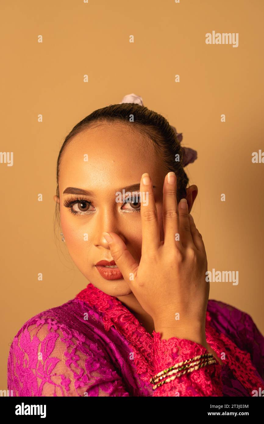 Portrait of Balinese woman with pink dress pose with hands on the face ...