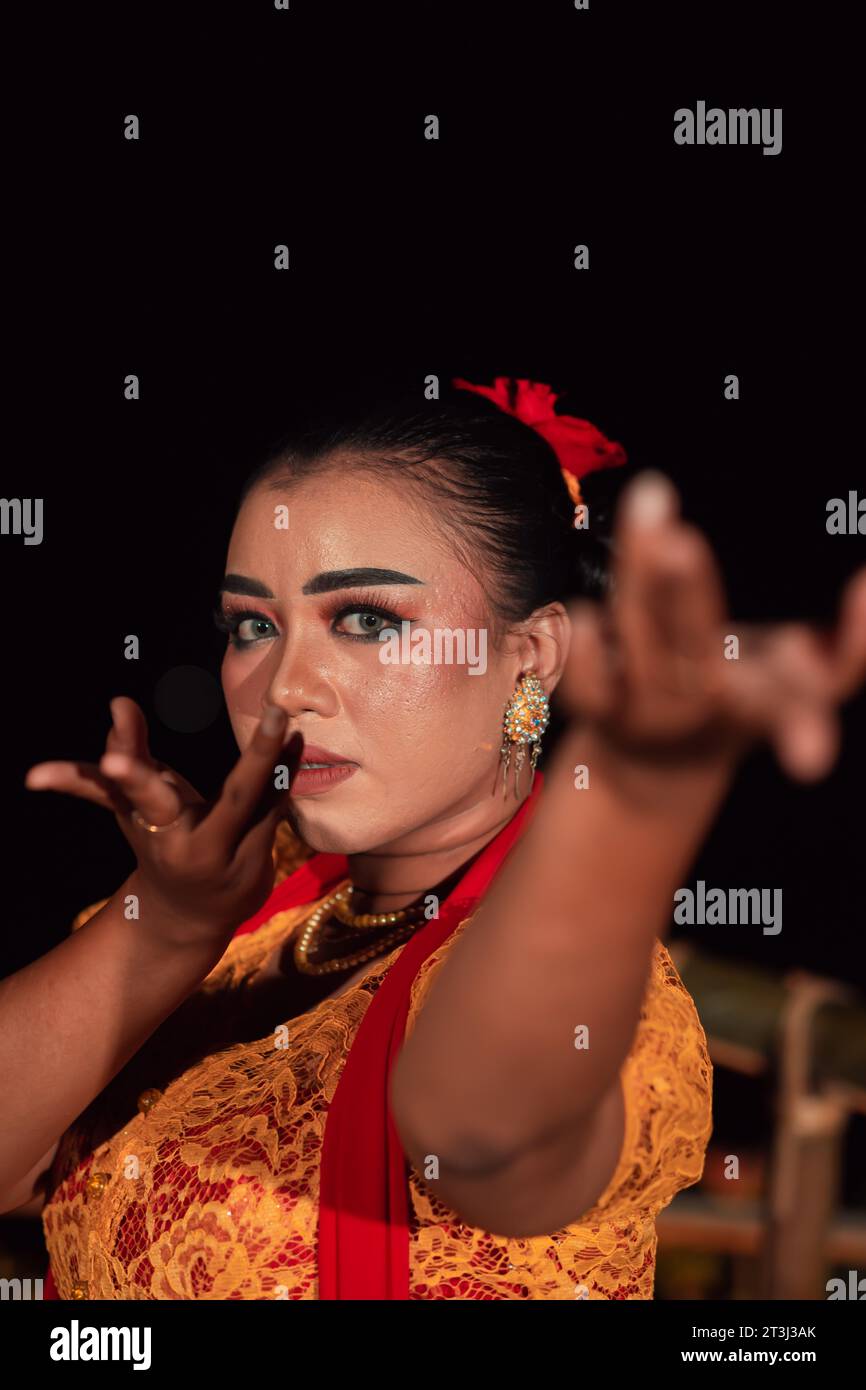 the fierce face of a Balinese woman with makeup in a traditional orange ...