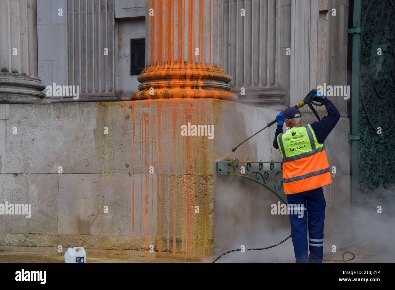 London, UK. 25th October 2023. A worker cleans the orange paint sprayed ...