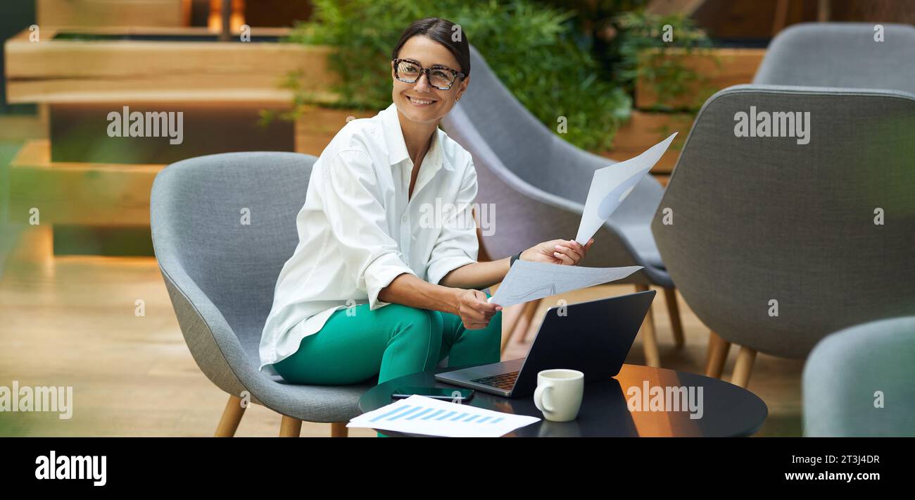 Smiling female analyst working with documents and use laptop in office ...