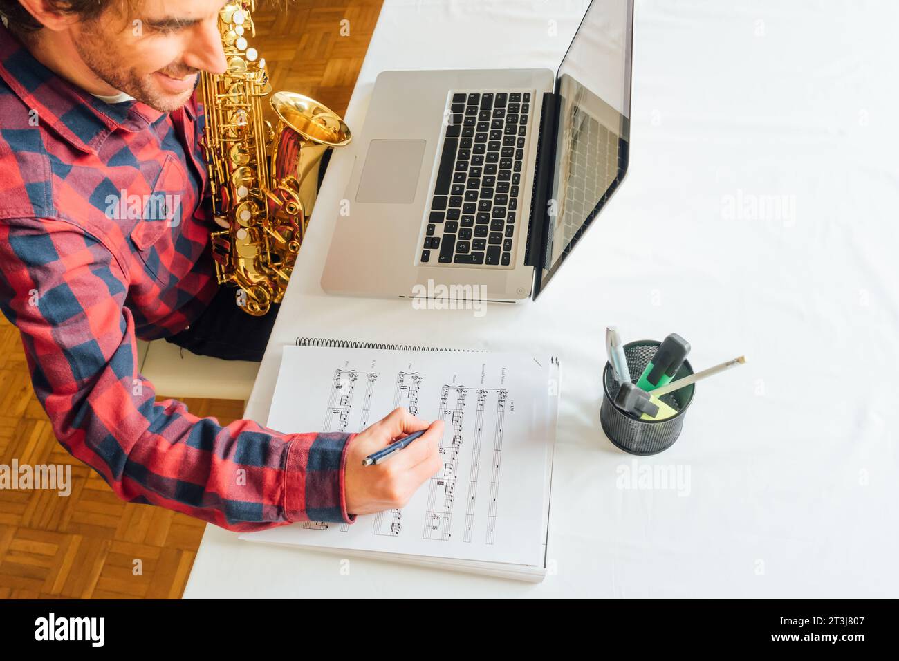 man making notes on sheet music while taking his saxophone online ...