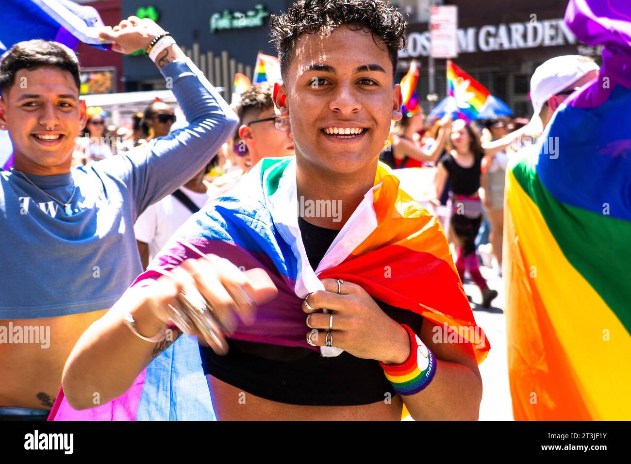 Smiling young adult man with gay pride flag draped over his shoulders ...