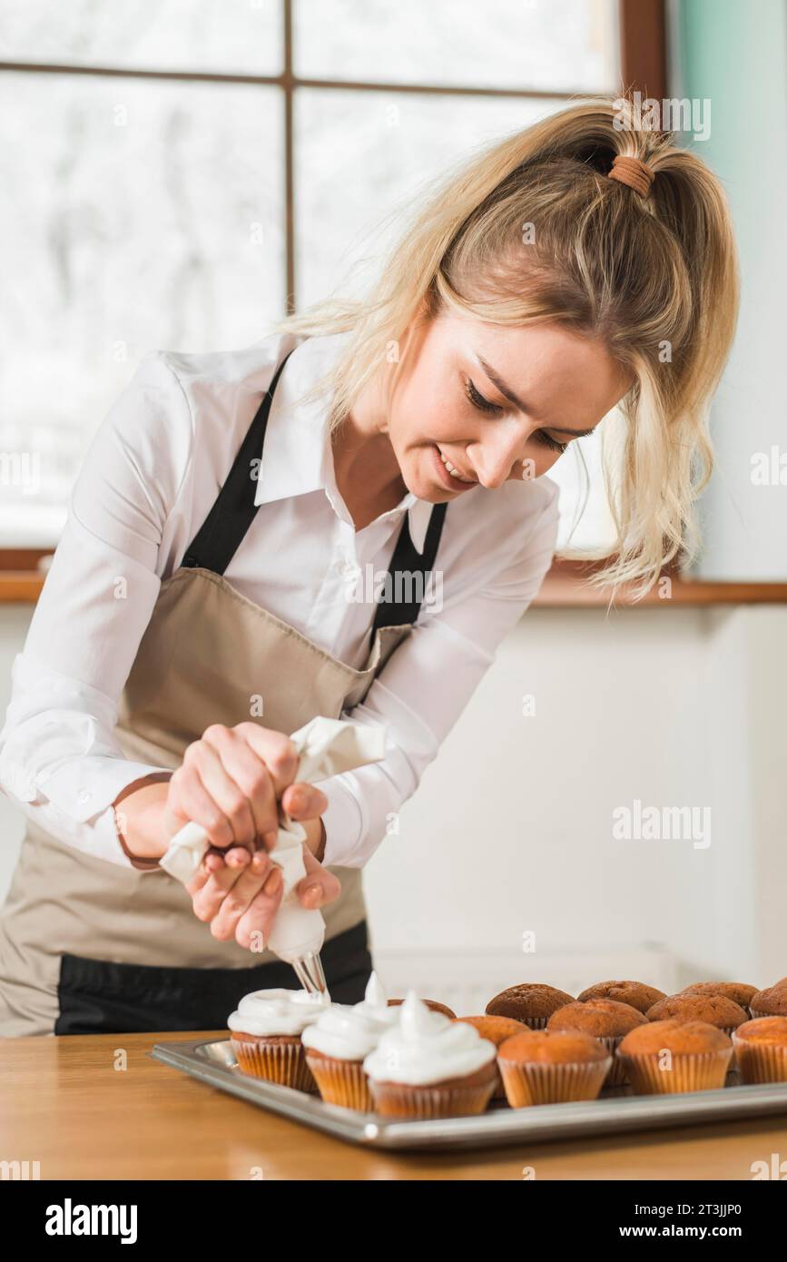 Female baker decorating cupcake with white butter cream by squeezing ...