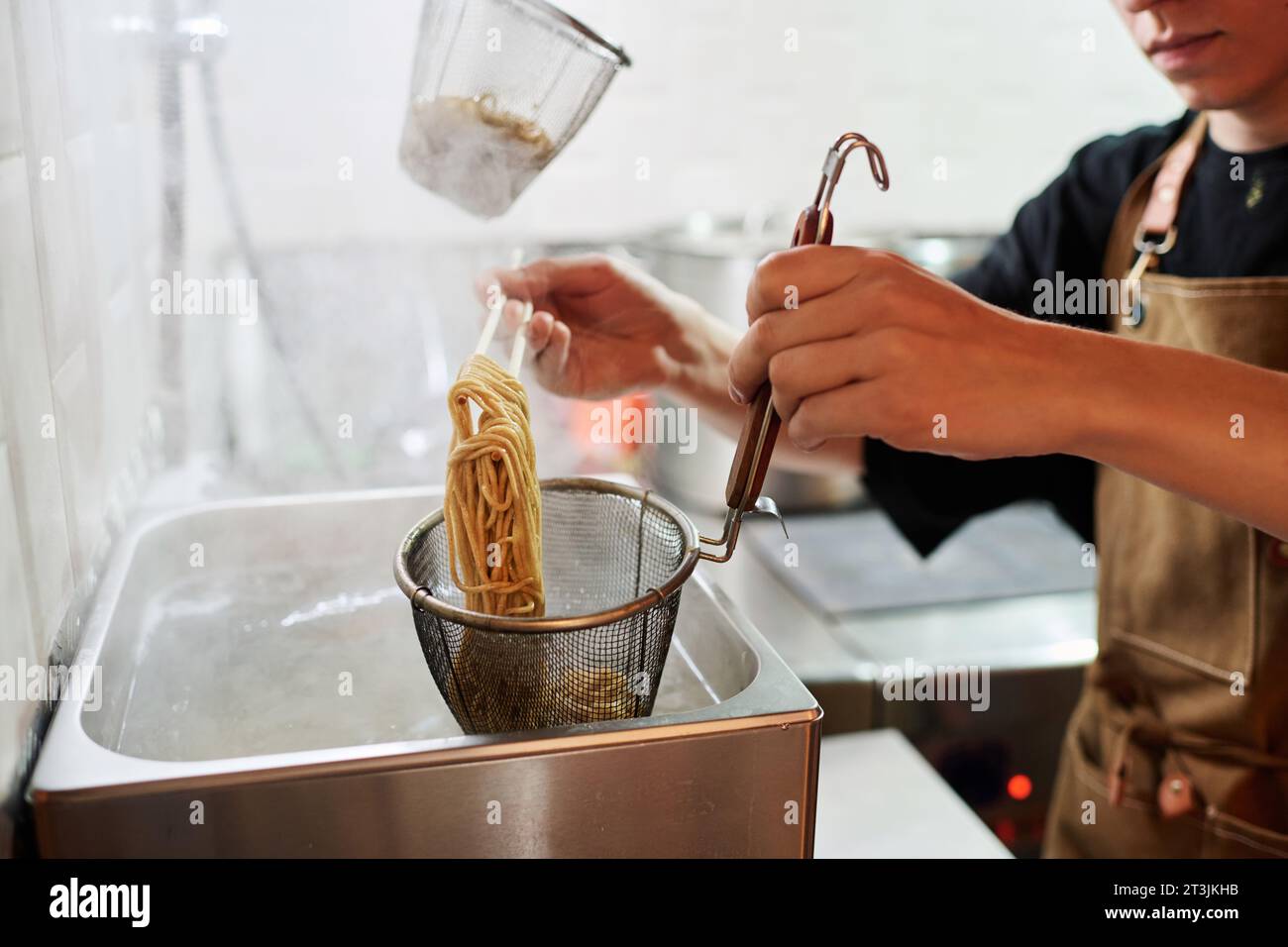 Young chef in apron putting hot boiled ramen into colander over ...