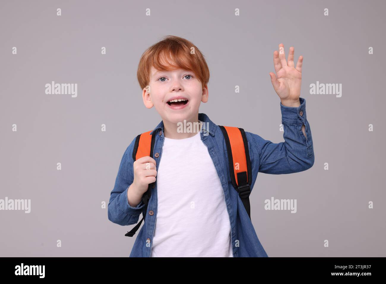 Happy schoolboy waving hello on grey background Stock Photo - Alamy