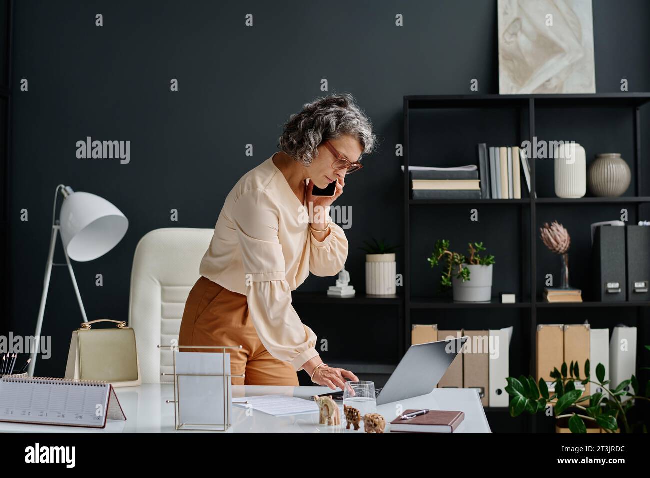 Side view of busy mature female boss with smartphone by ear bending ...