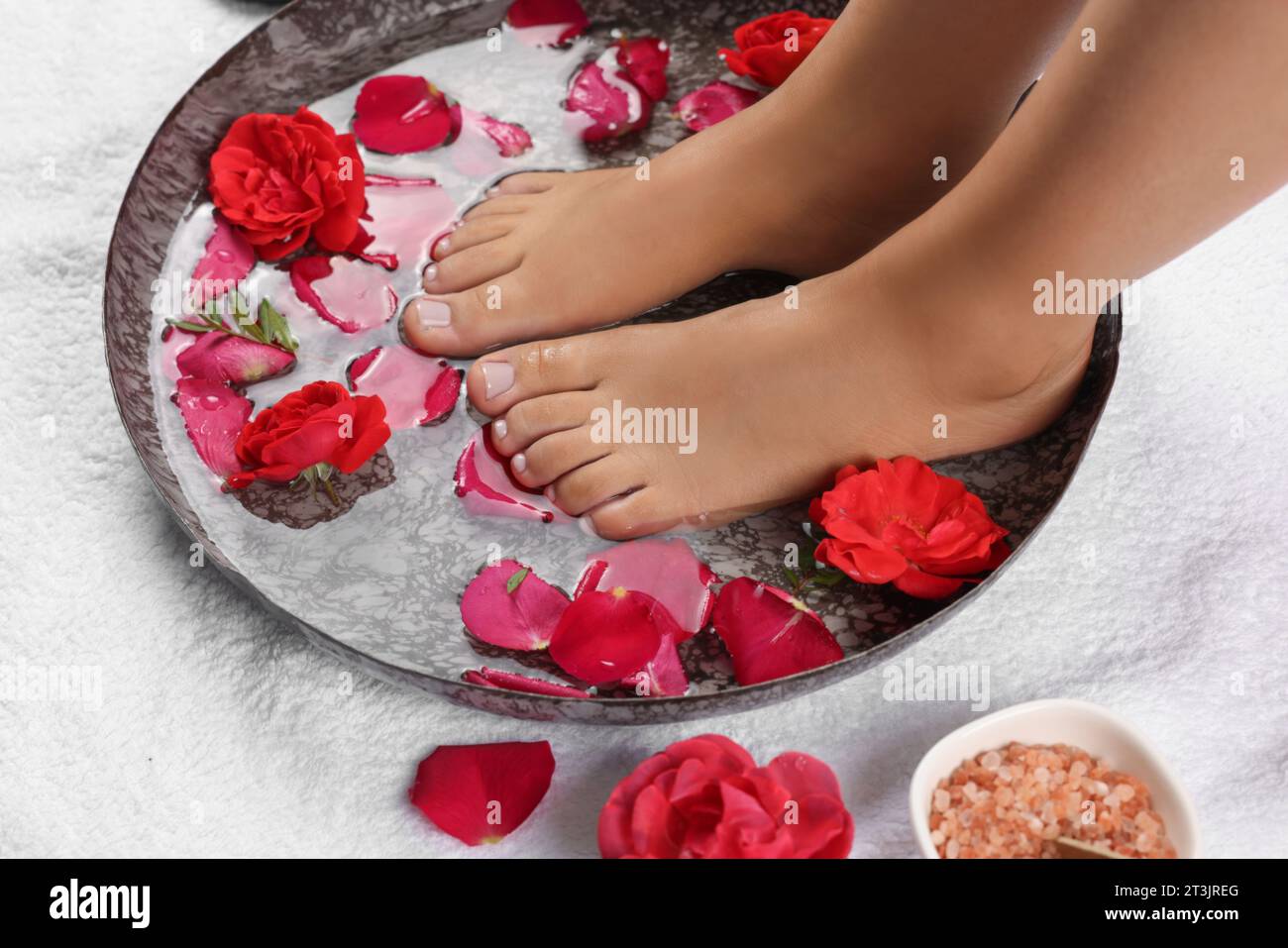 Woman soaking her feet in plate with water and red rose petals on white ...
