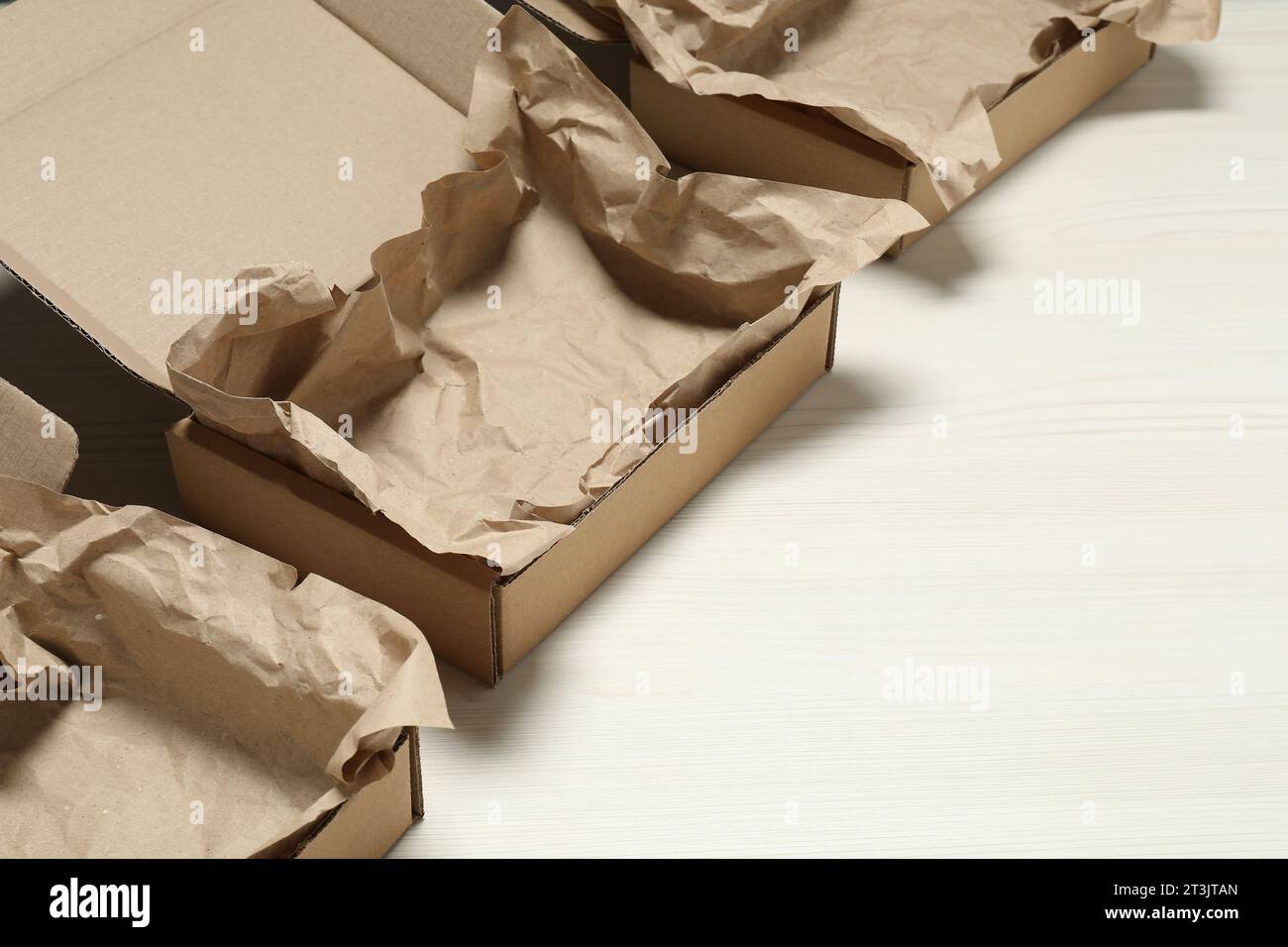 Open cardboard boxes with crumpled paper on white wooden floor. Space ...