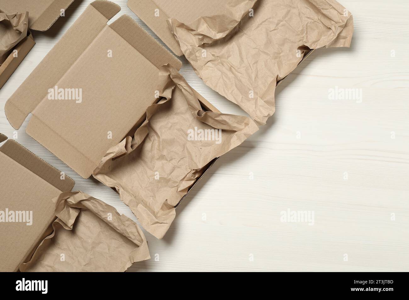 Open cardboard boxes with crumpled paper on white wooden floor, flat ...