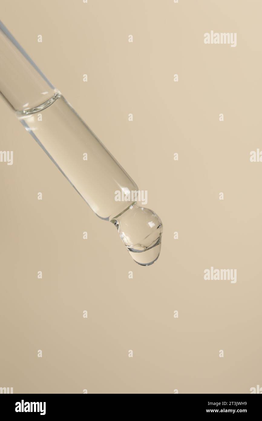 Dripping cosmetic serum from pipette on beige background Stock Photo ...