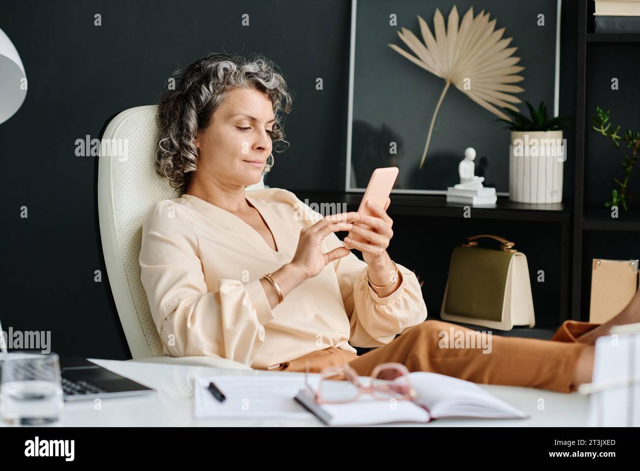 Mature relaxed female ceo in quiet luxury attire using mobile phone ...