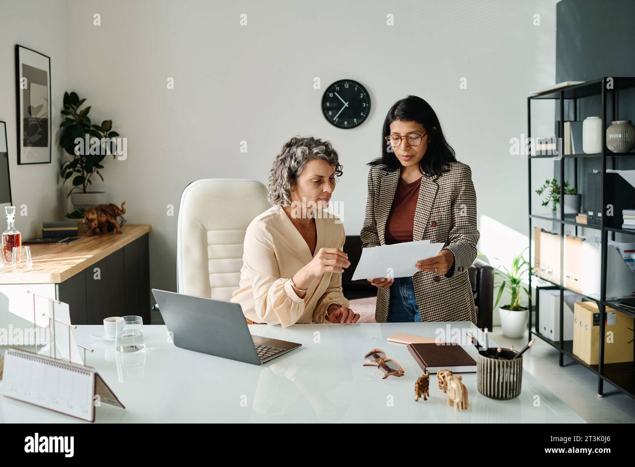 Mature female boss looking through documents held by young Hispanic ...