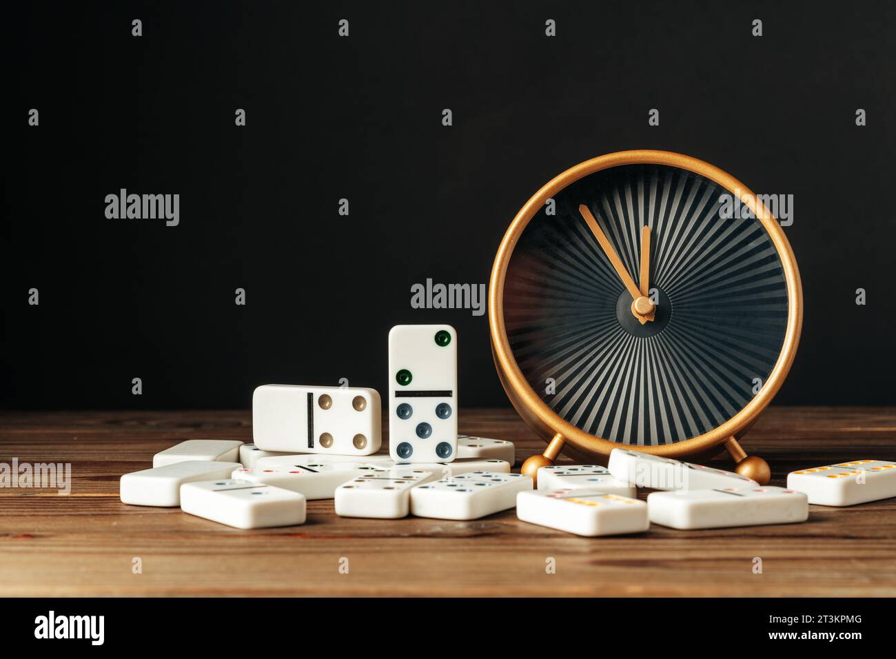 Domino tiles and clock on wooden table against black background Stock ...