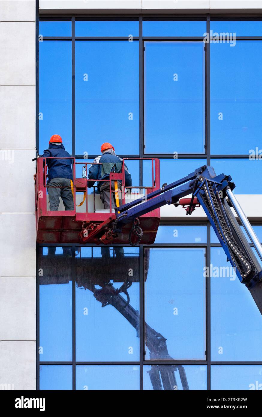 Two window cleaners clean the glass windows of a building at height on ...
