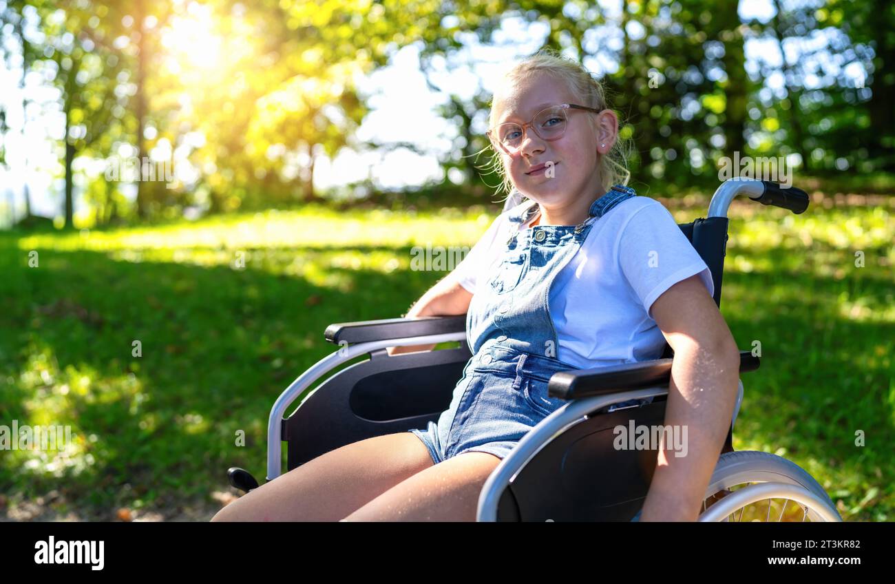 Happy young handicapped blond girl sit in wheelchair during walk in ...