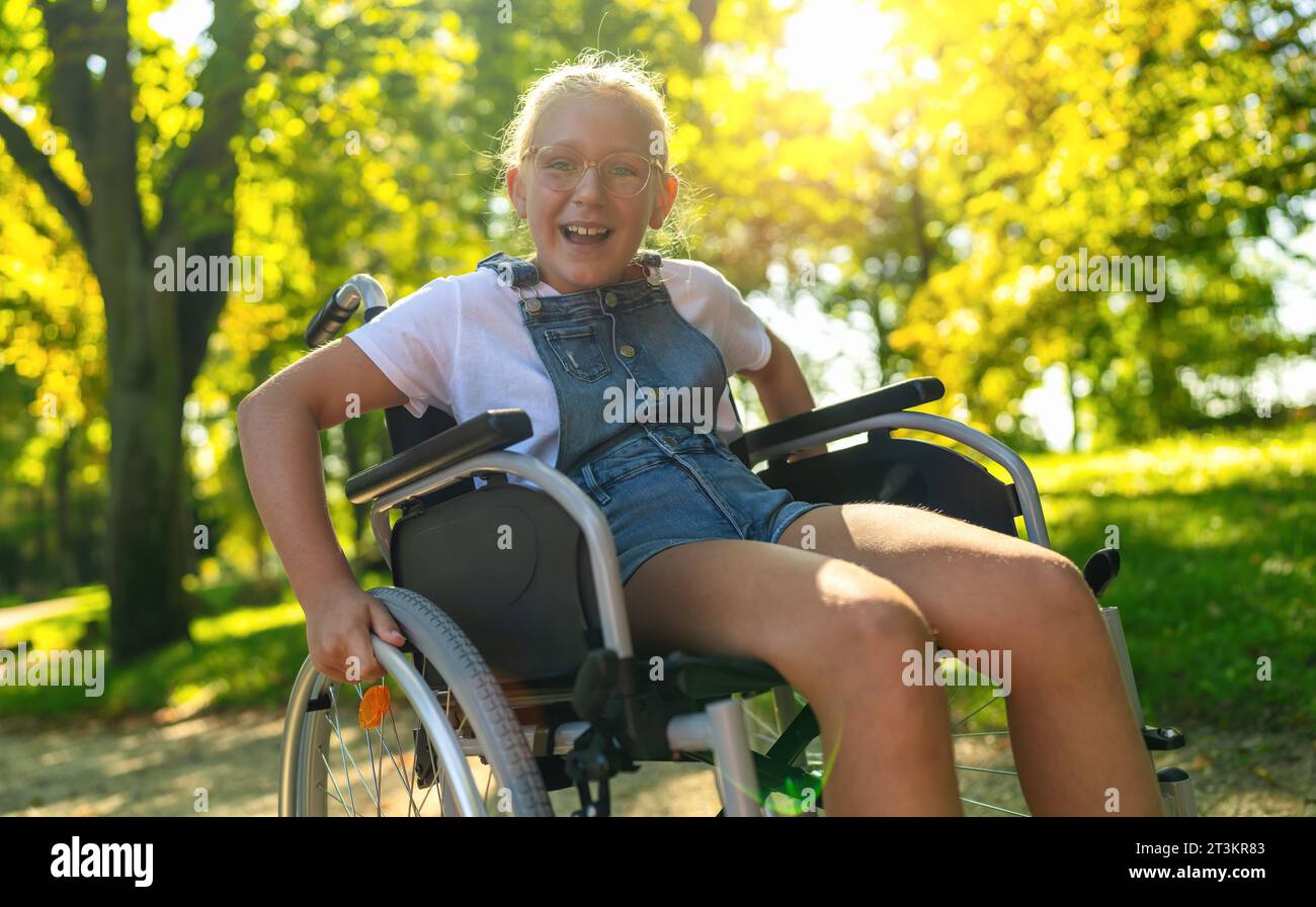 Happy young handicapped blond girl sit in wheelchair during walk in ...
