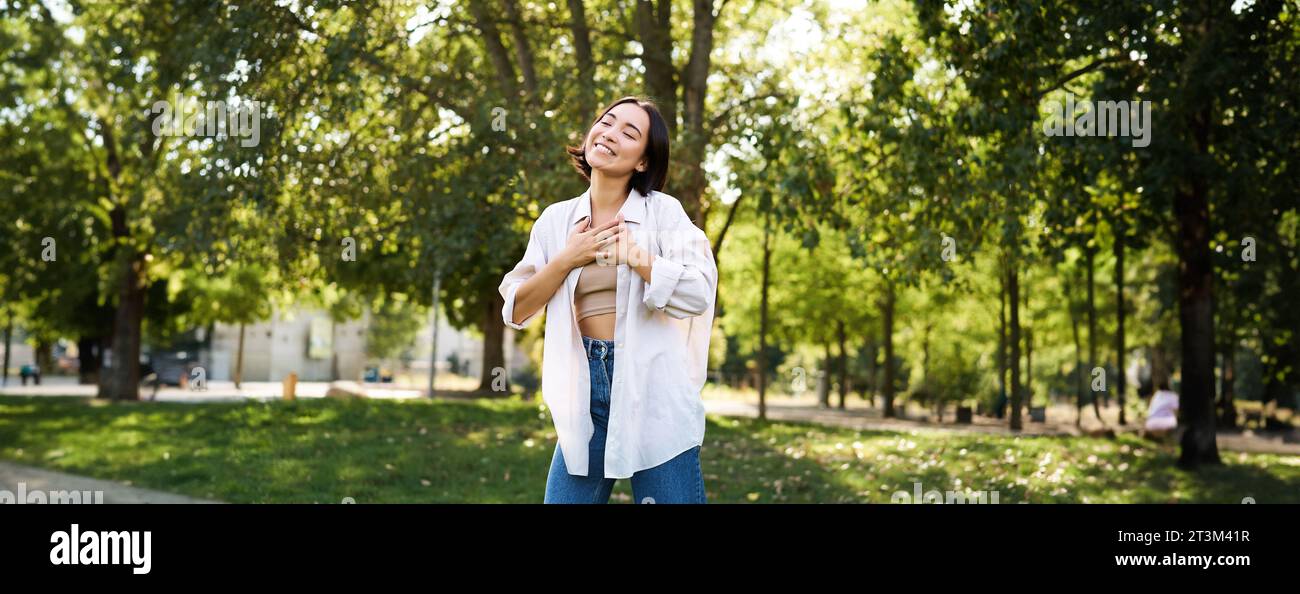 Happy young asian woman walking alone, dancing and singing in park ...