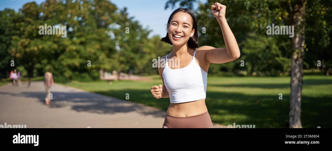 Happy fitness girl achieve goal, finish marathon, running with hands up ...