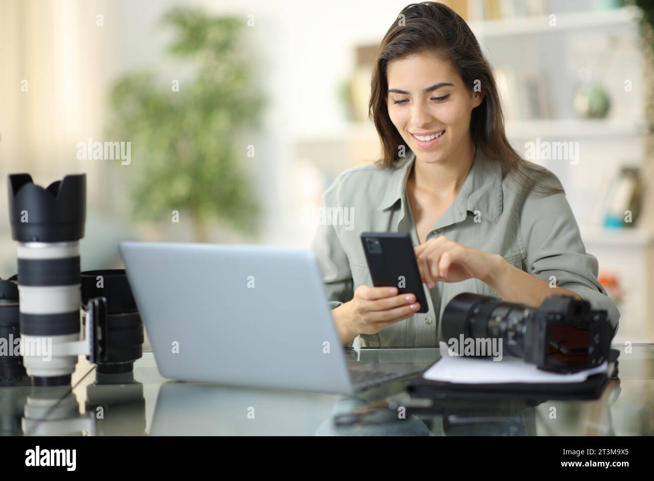 Happy photographer with laptop and cameras checking phone at home Stock ...