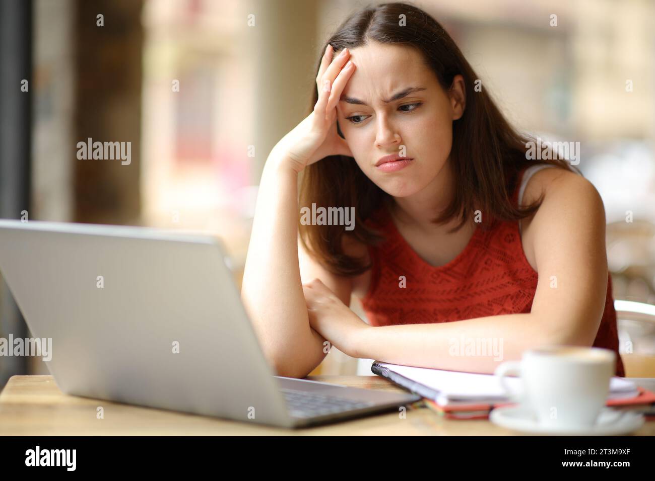 Frustrated student checking content on laptop in a coffee shop terrace ...