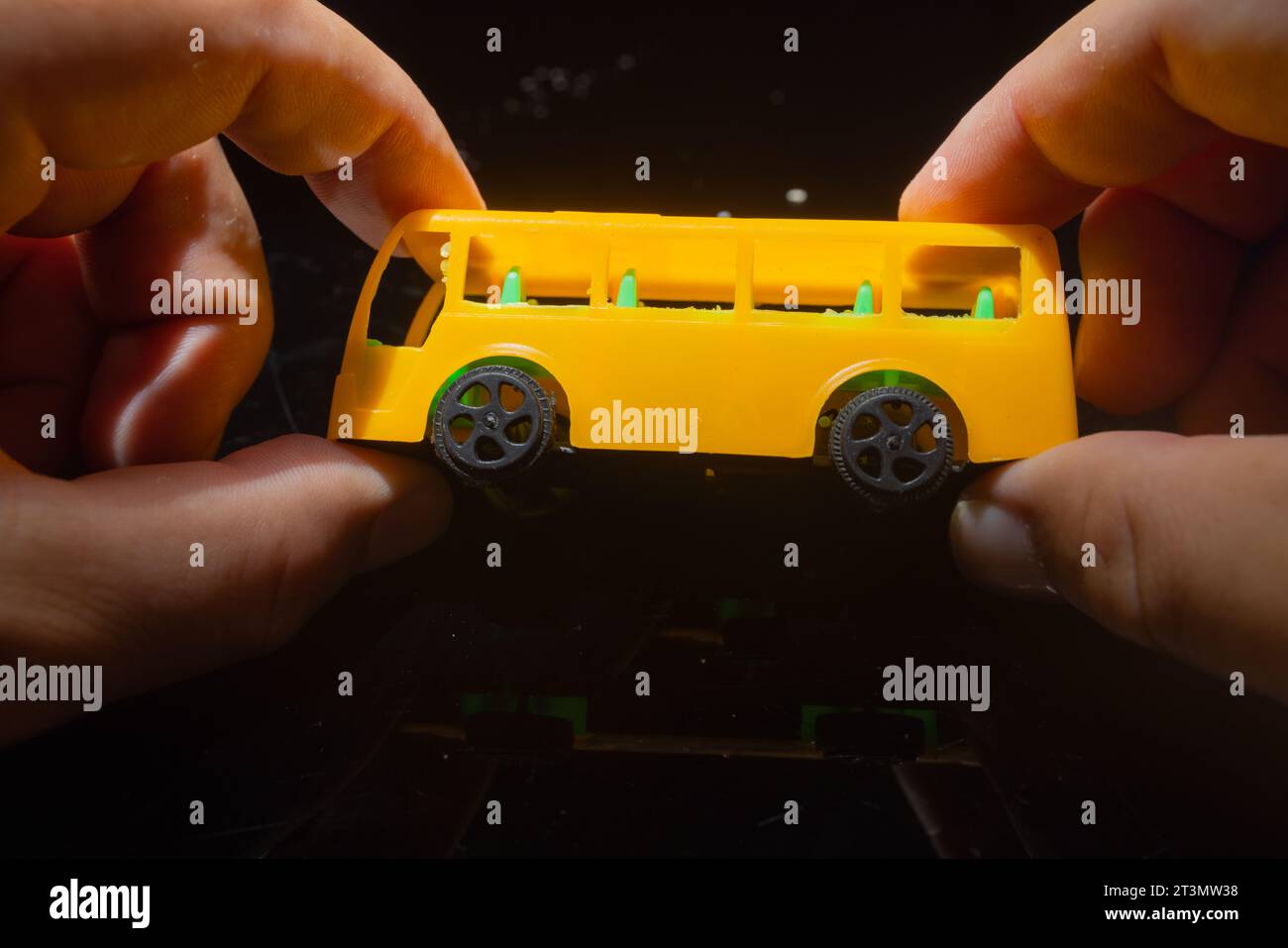 A man holds a plastic model of a yellow school bus, showcasing a ...