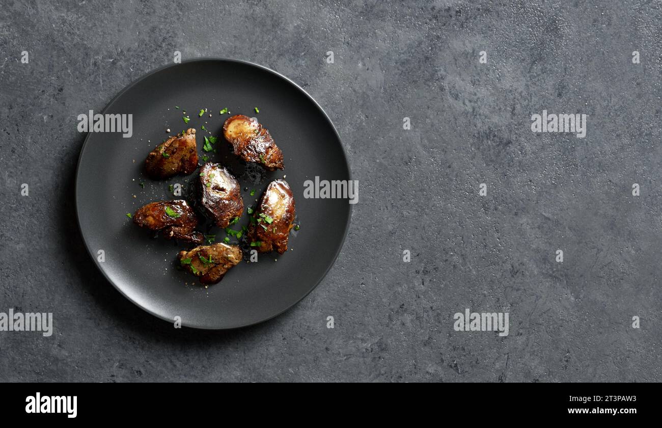 Roasted chicken liver on plate over dark stone background with copy ...