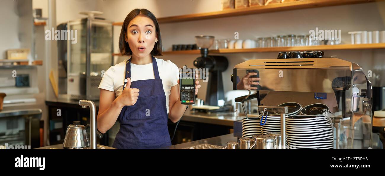 Portrait of cafe barista, girl shows thumbs up and card reader paying ...