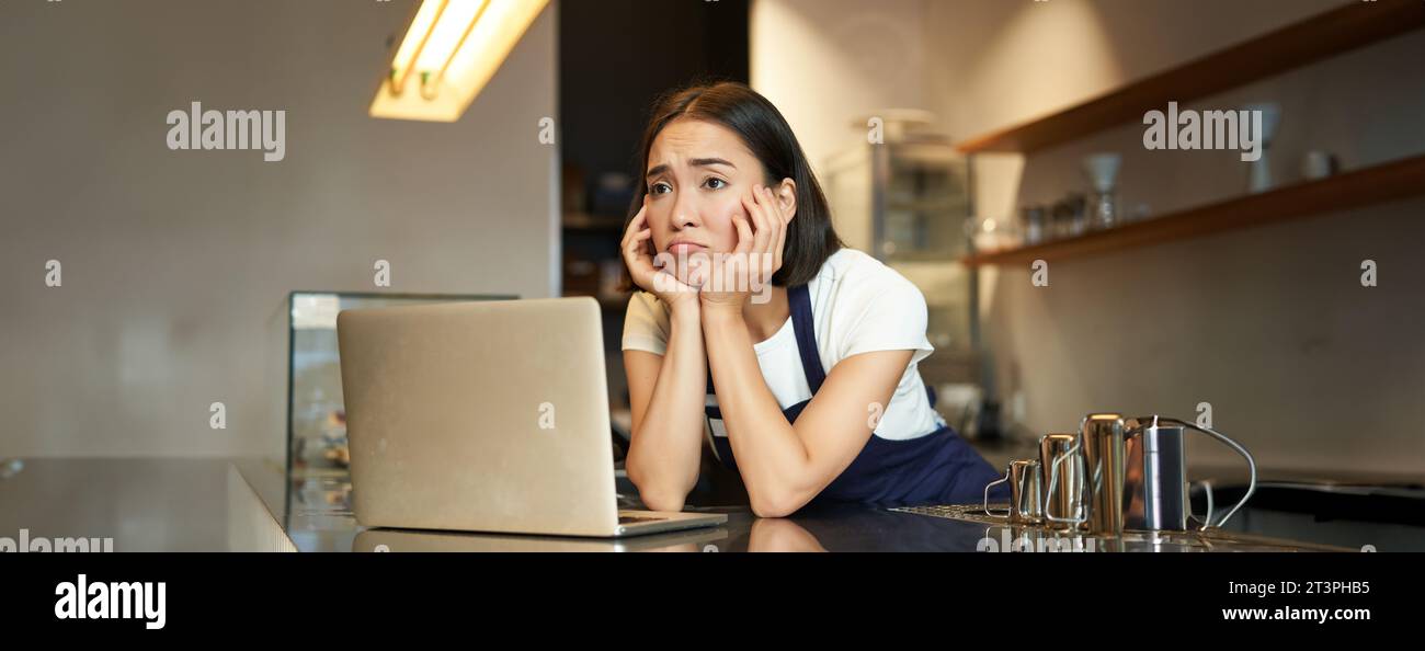 Asian girl barista, standing behind counter in cafe, looking as at ...