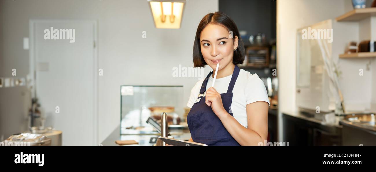 Smiling cute barista girl, korean woman working in cafe, using tablet ...