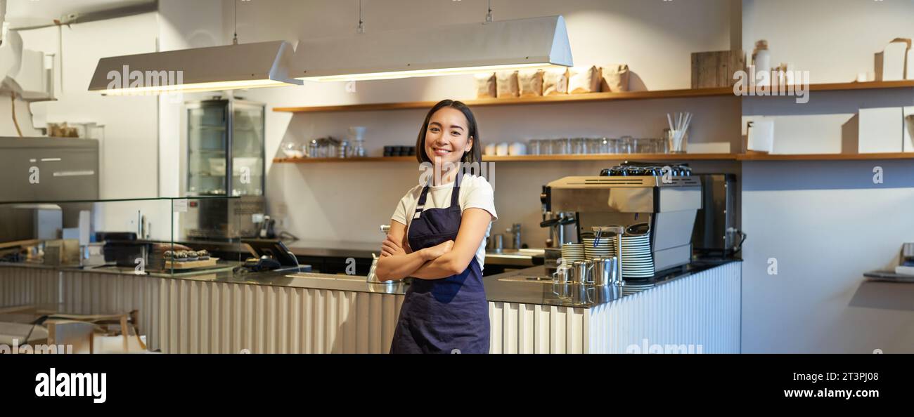 Portrait of cute asian woman barista, cafe staff standing near counter ...