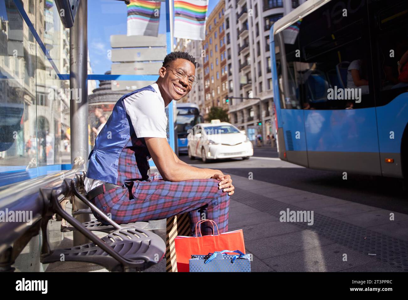 young African American man sitting at the bus stop with shopping bags ...