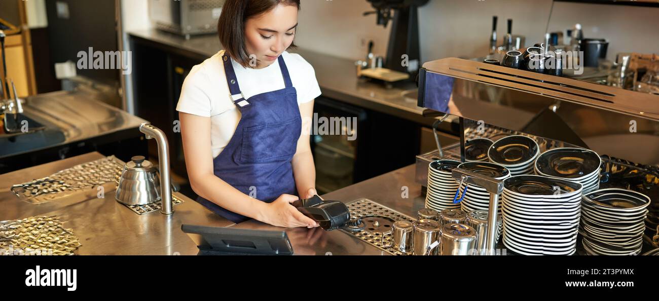 Smiling asian girl barista working in cafe at counter, processing ...