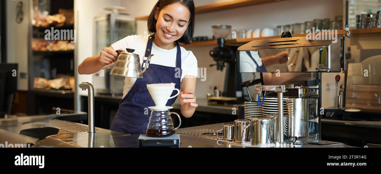 Cute brunette girl barista, cafe staff pouring water from kettle and ...