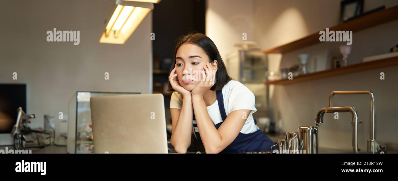 Asian girl barista, standing behind counter in cafe, looking as at ...