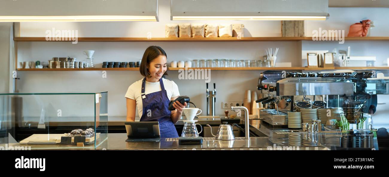 Portrait of cute girl student works as barista, holds POS credit card ...