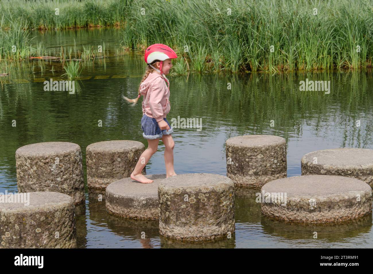 child caucasian girl crossing the water on the steps. girl is barefoot ...