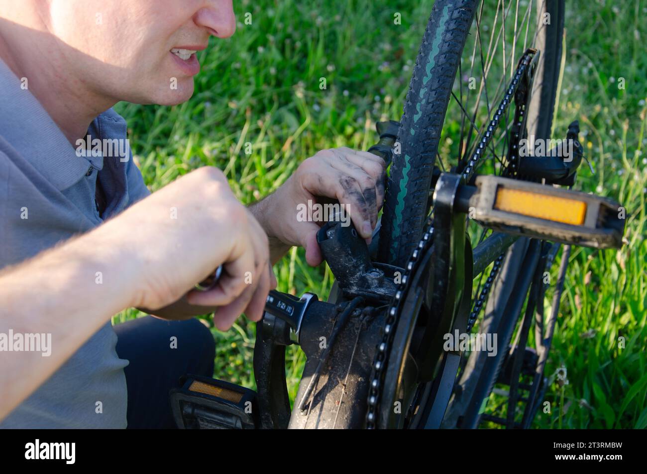 man repairing a bicycle chain in green park. Close-up shows hands and ...