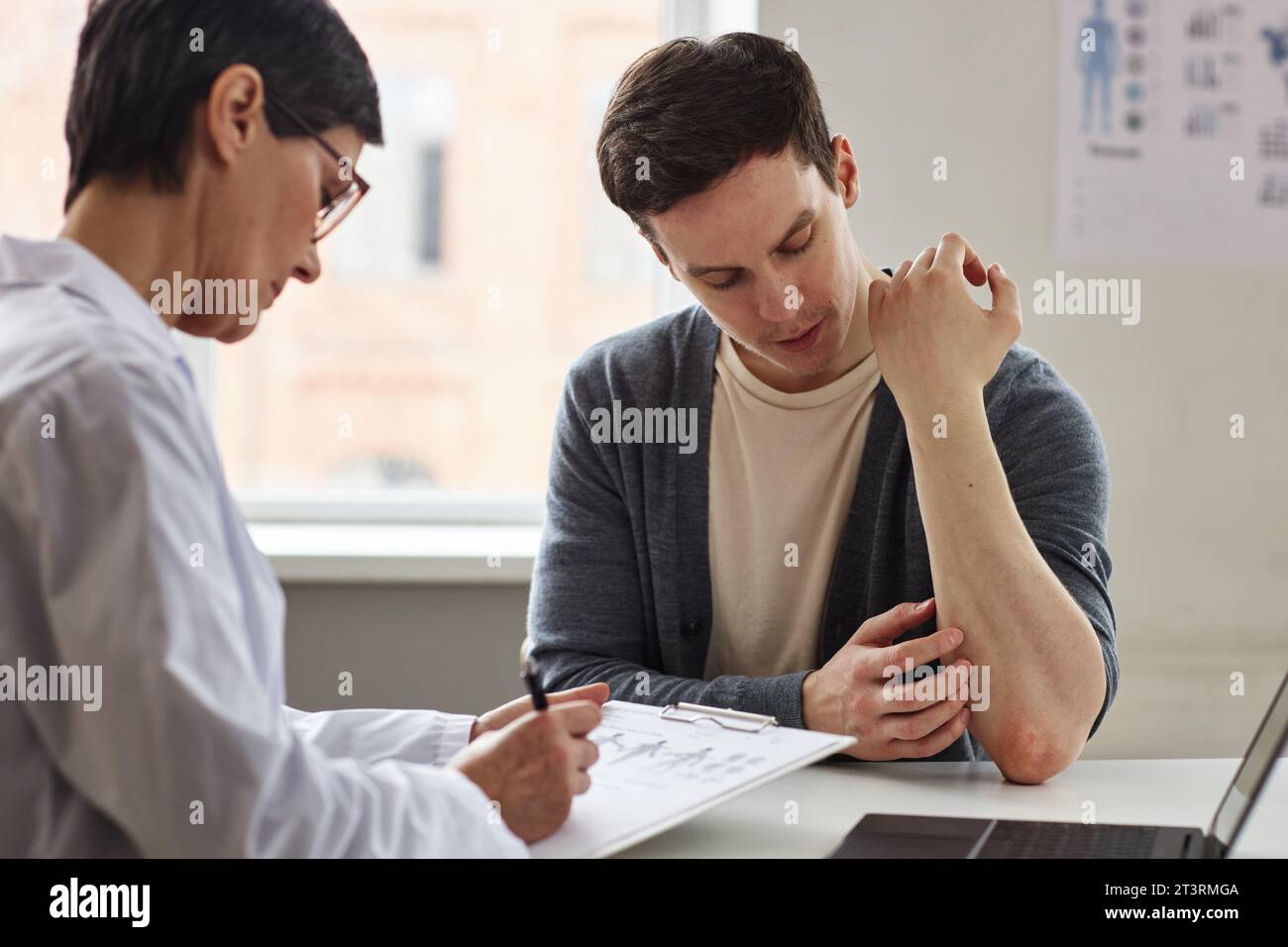 Portrait of young man showing skin rash to doctor during consultation ...