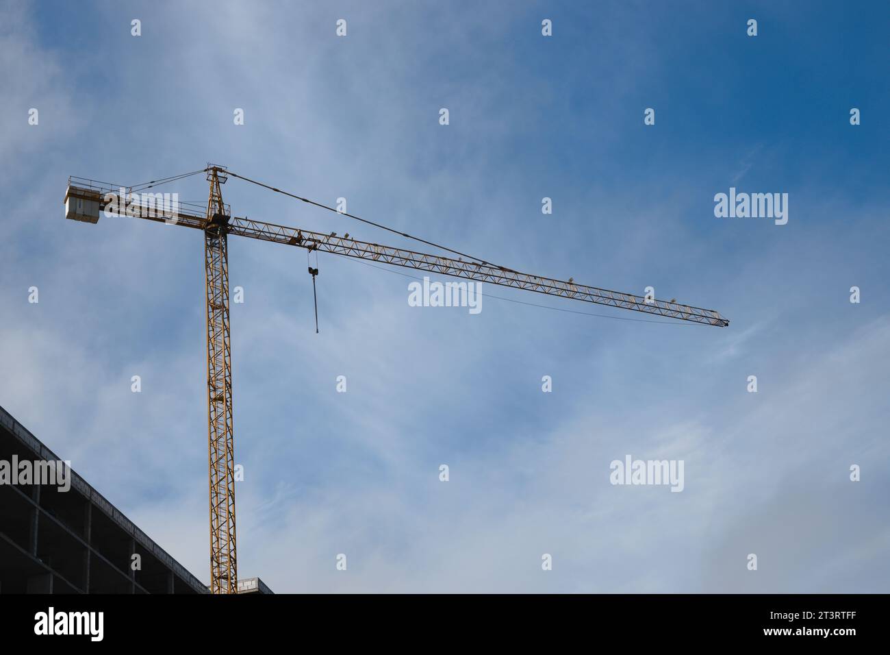 A tower crane at a construction site with a raised boom with blue sky ...