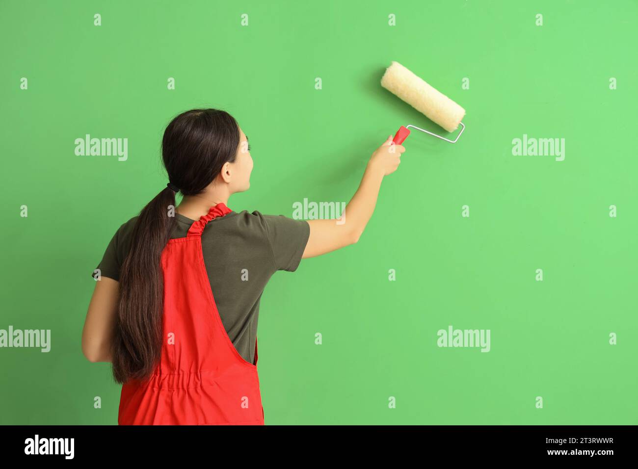 Female Asian decorator with paint roller on green background, back view ...