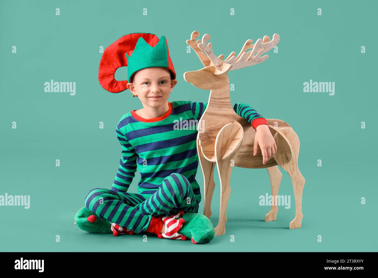 Cute little boy in elf costume with wooden reindeer on green background ...
