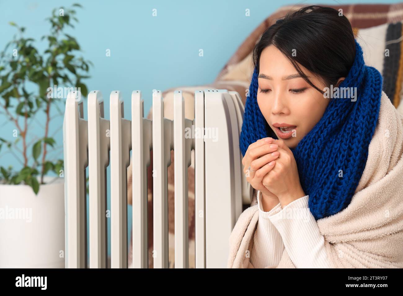 Frozen young Asian woman with radiator at home Stock Photo - Alamy