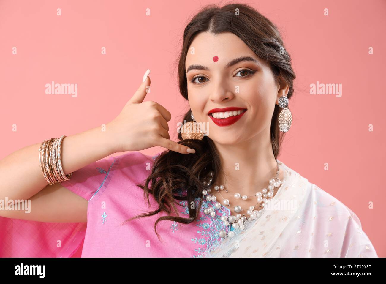 Beautiful young Indian woman in sari showing "call me" gesture on pink ...