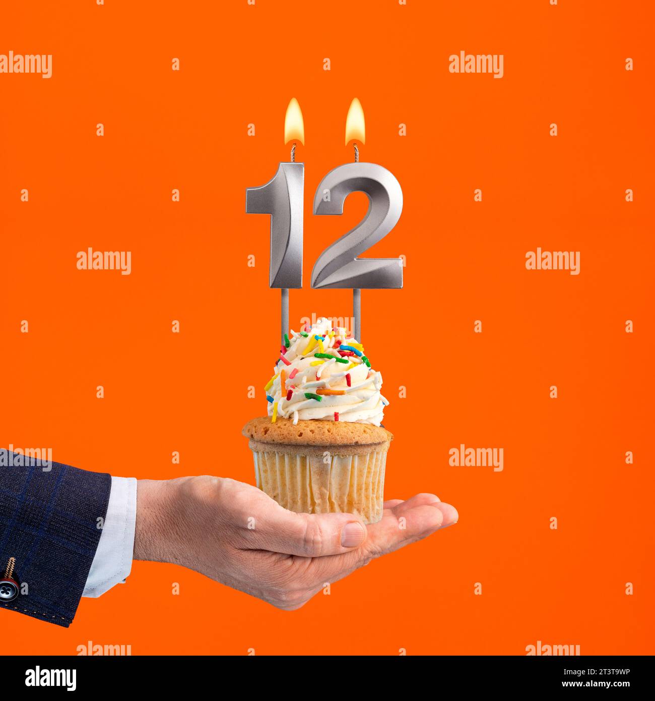 Hand holding birthday cupcake with number 12 candle - background orange ...