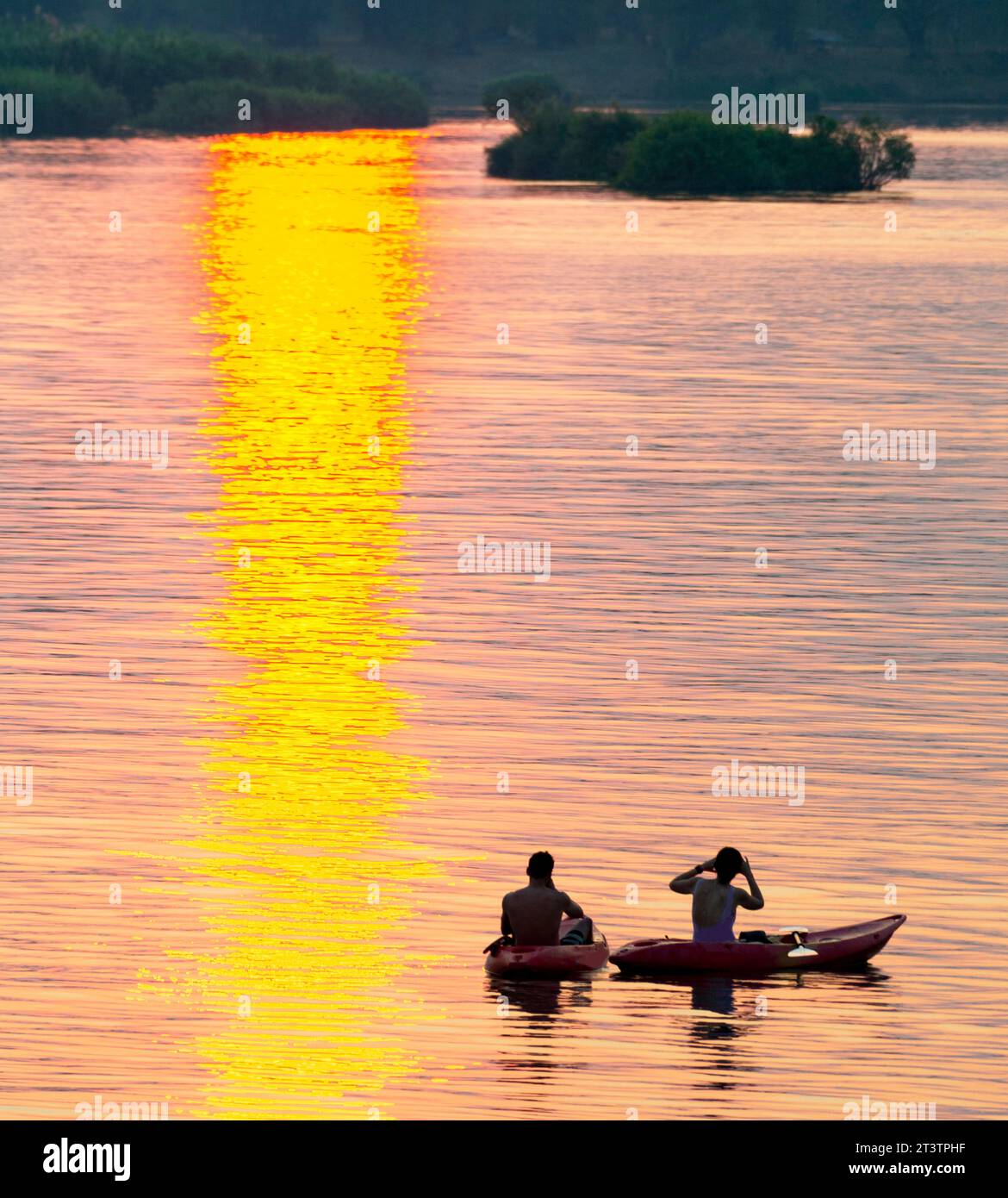 Silhouettes of two human figures in Kayaks,drifting across the calm ...