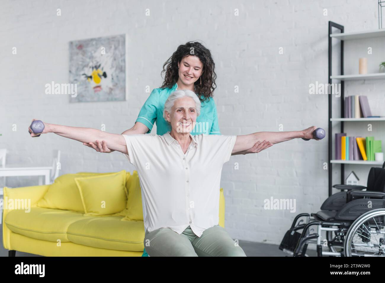 Female nurse assisting senior woman exercise with dumbbells Stock Photo ...