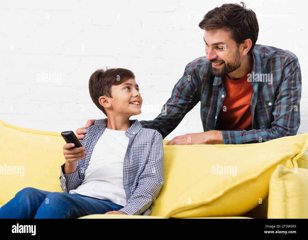 Son holding remote control looking his father Stock Photo - Alamy