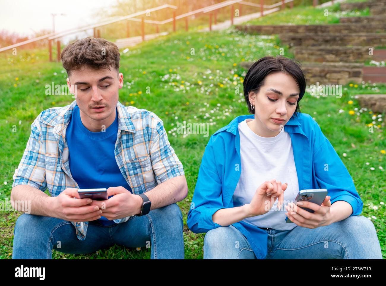 Sad couple using phones outdoors. A man peeps into a woman's phone ...