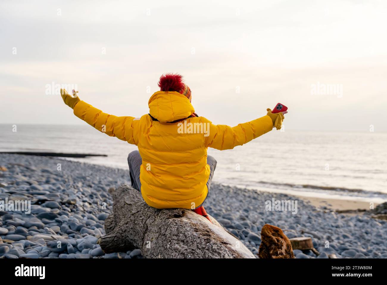 Woman in bright yellow jacket walking alone on the seaside on cold ...